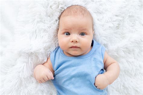自宅の白いベッドの上に青いボディスーツを着た生後3か月のかわいい男の子のポートレート 赤ちゃんのストックフォトや画像を多数ご用意