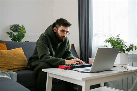 Man Recording Electronic Music Track With Portable Midi Keyboard On Laptop Computer In Home