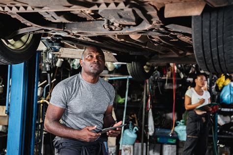두 명의 정비사가 차고에서 자동차 아래의 부품을 검사하고 체크리스트에 올립니다 남자에 대한 스톡 사진 및 기타 이미지 남자 흑인 민족 기계류 Istock