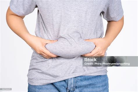 아시아 뚱뚱한 여성은 청바지에 과체중입니다 흰색 배경에 격리된 과도한 뱃살을 들고 있는 여자의 손 수술과 피하 지방 분해의 개념