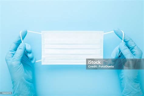 파란색 테이블 배경에 입과 코를 덮기 위해 흰색 호흡보호마스크를 들고 있는 고무 보호 장갑을 착용한 의사의 손 바이러스 시간의