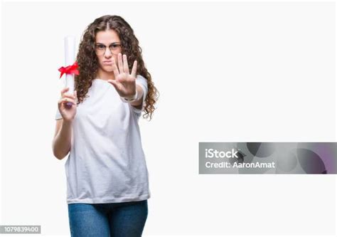 젊은 갈색 머리 여자 오픈 손으로 하 고 심각 하 고 자신감 표현 방어 제스처와 정지 신호 절연된 배경 위에 안경 착용 하 고 학위를 들고 갈색 머리에 대한 스톡 사진 및