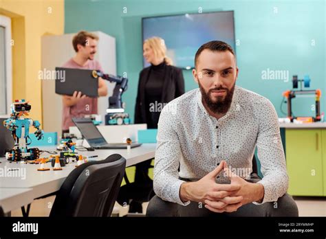A Man Sitting In A Robotics Laboratory While His Colleagues In The