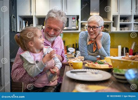 Grandpa Holding His Granddaughter In A Lap In A Kitchen With Grandma