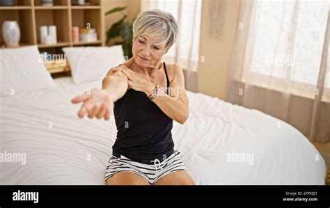 Mature Woman Applying Lotion On Her Arms While Sitting On A Bed In A
