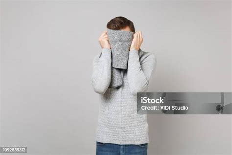 스튜디오에서 회색 벽 배경에 고립 된 스카프로 얼굴을 덮고 회색 스웨터에 있는 젊은이의 초상화 건강 패션 라이프 스타일 사람들이