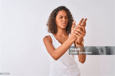 고립 된 흰색 배경 위에 서있는 캐주얼 한 티셔츠를 입은 젊은 브라질 여성은 손과 손가락에 통증 관절염 염증을 앓고 있습니다