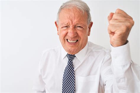 고립 된 흰색 배경 위에 서있는 넥타이를 입은 선임 회색 머리 사업가는 화가 나고 화가 나서 분노로 외치고 미친 듯이 소리지르고