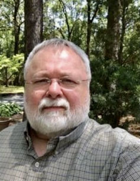 An Older Man With Glasses And A Beard Standing In Front Of Some Trees