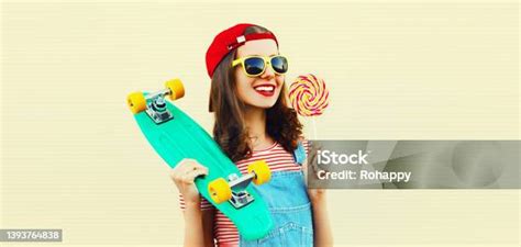 하얀 배경에 야구 모자를 쓰고 롤리팝과 녹색 스케이트 보드를 가진 행복한 미소 짓는 젊은 여성의 여름 초상화 20 29세에 대한 스톡 사진 및 기타 이미지 Istock