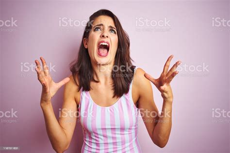 분홍색 고립 된 배경에 줄무늬 핑크 수영복 수영복을 입고 젊은 아름다운 여성은 미친 미친 소리와 공격적인 표정과 팔을 들고 고함