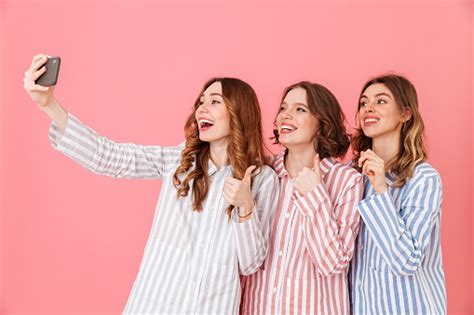 핑크 배경에 고립 된 행복한 수면 중에 휴대 전화를 사용하여 재미있게 셀카를 찍는 다채로운 줄무늬 잠옷을 입은 3 명의 귀여운