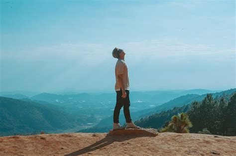 背景に青い空と山々を見上げるベージュのシャツと黒のズボンを着た男：無料の写真素材