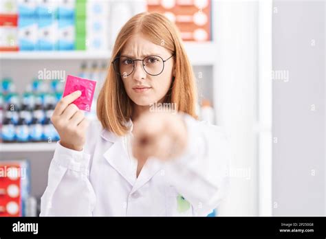Junge rothaarige Frau in einer Apotheke arbeitet und ein Kondom hält mit dem Finger auf