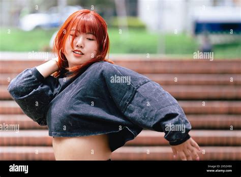 Korean Woman With Fiery Red Hair Caught In A Spontaneous Dance Moment On City Steps Stock Photo