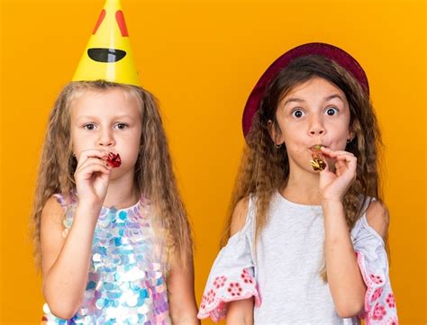 Joyeuses petites jolies filles avec des chapeaux de fête soufflant des