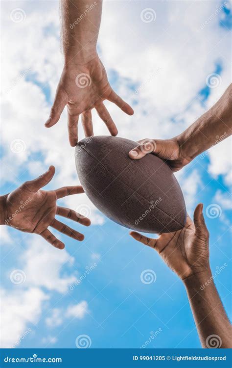 Hands Holding American Football Ball On Background Of Blue Sky Stock
