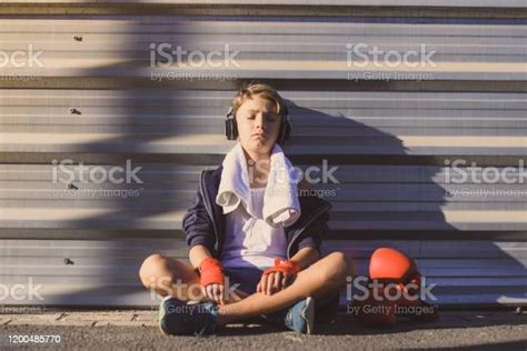 그의 손에 권투 밴드와 잘 생긴 젊은 남성 경기 전에 휴식 도로에 앉아 소년 상자 운동 듣기 음악에 대 한 준비 스포츠 청소년 결단력 및 경쟁 개념 땀에 대한 스톡 사진 및