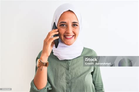 행복한 얼굴 서서 치아를 보여주는 자신감 미소와 함께 미소와 고립 된 배경을 통해 스마트 폰에 말하는 히잡을 입고 젊은 아랍 여성 건강한 생활방식에 대한 스톡 사진 및 기타