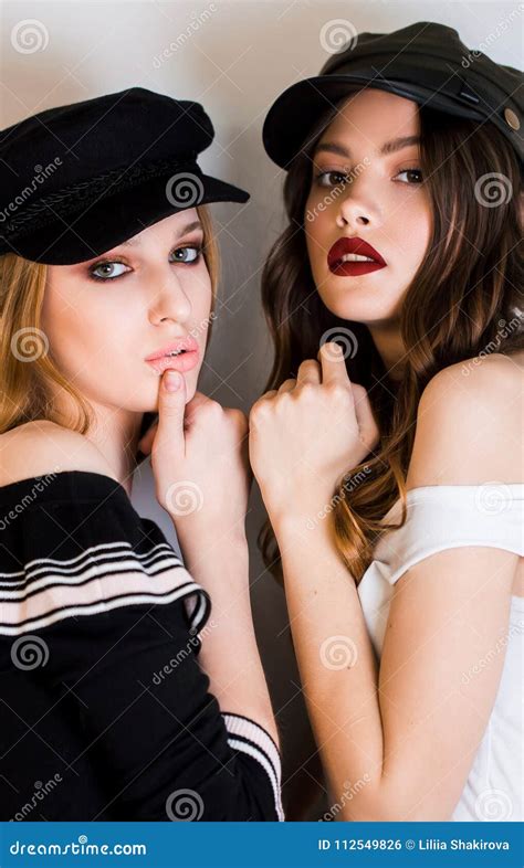Two Beautiful Women Blonde And Brunette Girls In Black Caps And Bright