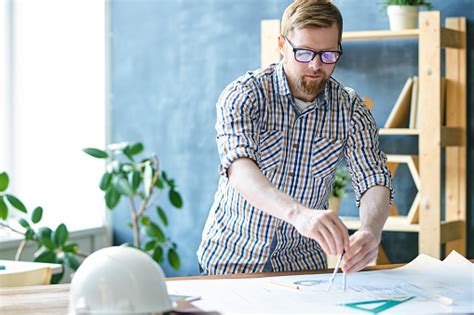 책상에 서 있는 안경에 숙련 된 젊은 건설 엔지니어가 집중 하 고 청사진에 원을 그리는 기술 나침반을 사용 하 여 건설 산업에 대한 스톡 사진 및 기타 이미지 Istock