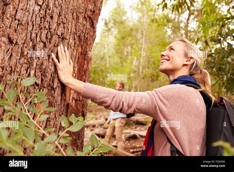 Woman Touching A Tree In A Forest Husband In The Background Stock Photo Alamy