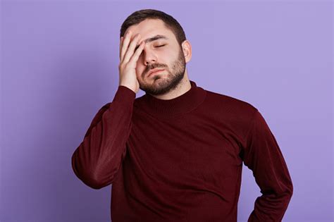 수염과 검은 머리를 가진 지친 화가 남자의 실내 촬영 그의 눈을 감고 손으로 그의 얼굴을 만지고 피곤 라일락 배경 위에 고립 된