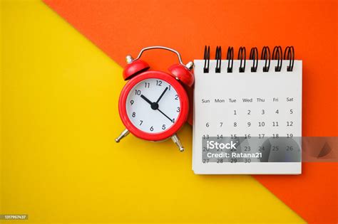 빨간색 아날로그 알람 시계와 흰색은 두 톤 노란색과 주황색 종이 배경 상단 보기에 흰색 열린 달력 개념에 대한 스톡 사진 및