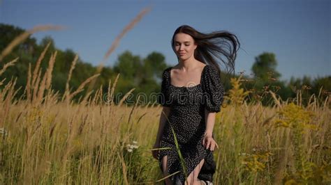 A Brunette Girl With Long Hair In A Black Dress Runs Across A Field On