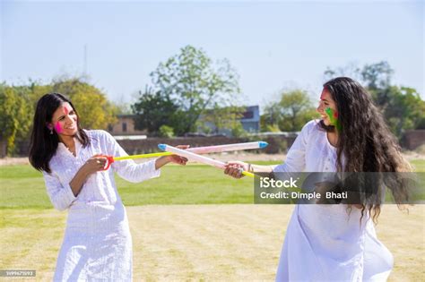 하얀 쿠르타 의상을 입은 두 명의 행복한 젊은 인도 여자 친구들이 공원에서 홀리 축제를 축하하는 피치카리와 놀고 있다 20 24