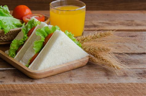 나무 접시에 토마토와 양상추 샌드위치 햄 치즈의 조각 수 제 샌드위치는 아침 이나 점심에 대 한 오렌지 주스와 함께 제공 됩니다 맛 있는 햄 치즈 샌드위치 화강암 테이블에