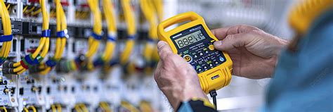 A Professional Electrician Using Digital Multimeter To Test An Electrical Panel Background