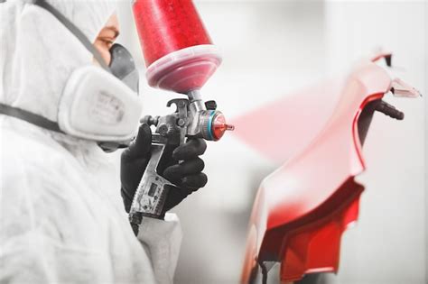 수리 작업 중 페인트 챔버에 스프레이 건으로 자동차 펜더를 칠하는 자동차 정비사 프리미엄 사진