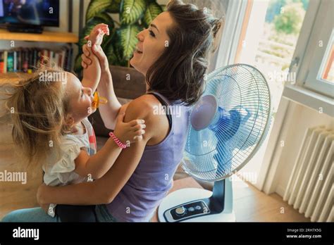 On A Hot Day A Mother And Her Young Daughter Turn The Cooling Fan Into