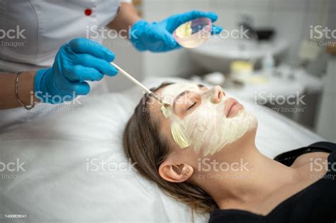 미용 살롱에서 얼굴 마스크를 만드는 의사 미용사 또는 피부과 의사 목욕 가운에 침대에 누워있는 백인 여성 얼굴에 얼굴 마스크를