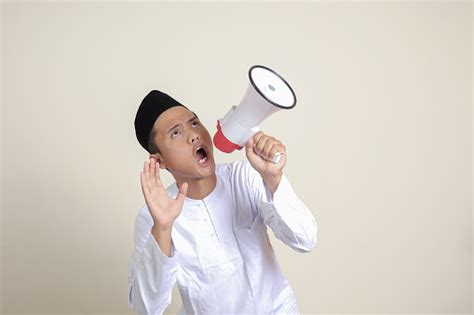 해골 모자를 쓴 흰 셔츠를 입은 매력적인 아시아 무슬림 남자의 초상화는 메가폰을 사용하여 더 크게 말하며 제품을 홍보합니다 광고