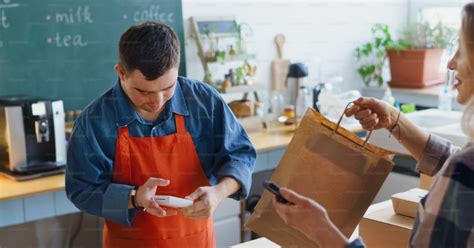 쾌활한 젊은 다운 증후군 웨이터가 테이크아웃 레스토랑에서 의상을 입은 비접촉식 스마트폰 결제를 하고 있다 사진 Unsplash의 미소 이미지