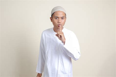 흰 셔츠를 입은 매력적인 아시아 무슬림 남자의 초상화는 악의적인 대화 대화를 속삭이고 입에 손을 대고 비밀 소문을 전한다 회색