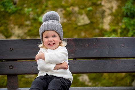 귀여운 금발 아이가 공원 밖에 벤치에 앉아 웃고 있다 봄날 야외에서 모자를 쓰고 있는 행복한 아이 사랑스러운 웃는 백인 소년은 놀이터에서 놀이 시간을 보낸 후 벤치에서 쉬고