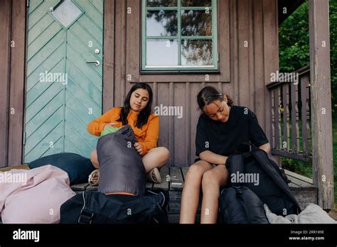 Girls Unpacking Backpacks While Sitting On Porch Outside Cabin Stock