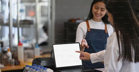 카운터 바 뒤에서 일하는 젊은 여성 커피 숍 주인은 메뉴를 추천하고 고객으로부터 주문을받습니다 사진 Unsplash의 디지털 태블릿 이미지