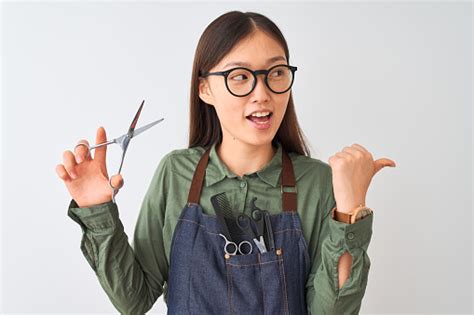 중국 미용사 여자 안경을 들고 가위를 들고 고립 된 흰색 배경 가리키는 고 행복 한 얼굴 미소와 함께 측면에 엄지 손가락으로