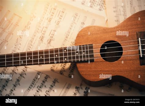 A Small Wooden Ukulele With Nylon Strings Lies On Scattered Sheets Of