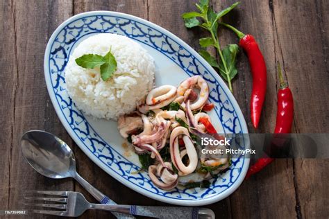 포크와 숟가락 카오 패드 카파오와 소박한 나무 배경에 흰색 접시에 바질 태국 길거리 음식 매운 볶음밥 그것은 오징어 달콤한 바질과 고추에서 요리 Pad Krapao에 대한
