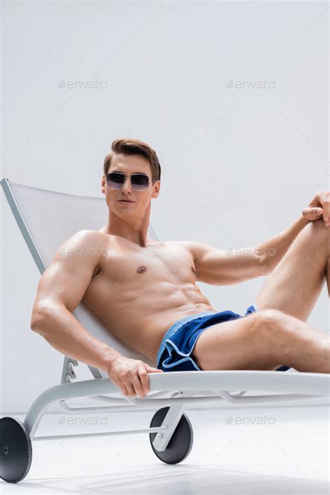 Sportive Man In Swimming Trunks And Sunglasses Sitting In Deck Chair