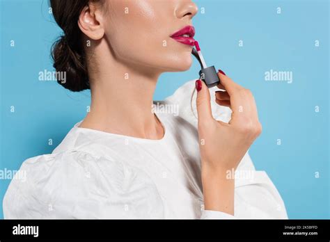 Cropped View Of Young Woman In Blouse Applying Pink Lip Gloss On Blue