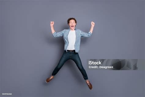 세련 된 최신 유행 잘 좋은 잘생긴 매력적인 행운 남자 캐주얼 체크 무늬 셔츠에 청바지 물결 모양 머리를 가진 승리를 축 하 하의 전체 길이 몸 크기입니다 회색 배경 위에