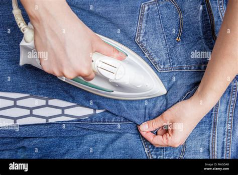 Image Of Man Ironing Blue Jeans On Ironing Board In Apartment Stock