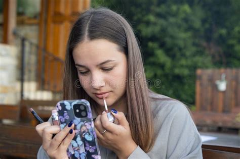 Young Girl Applying Lipstick While Looking At Herself In The Mirror Of