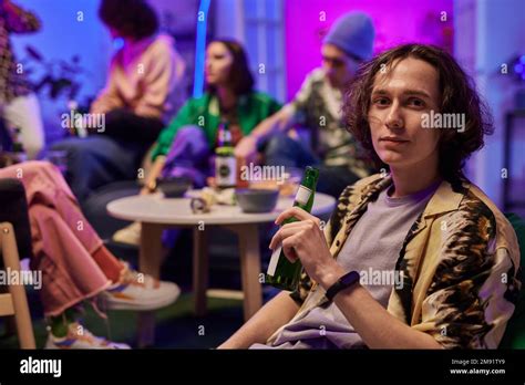 Junger Mann mit einer Flasche Bier in der Hand der auf der Party in Kamera schaut während